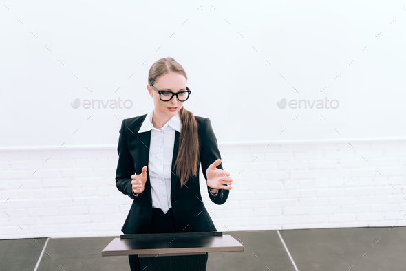attractive lecturer standing and gesturing at podium tribune during ...