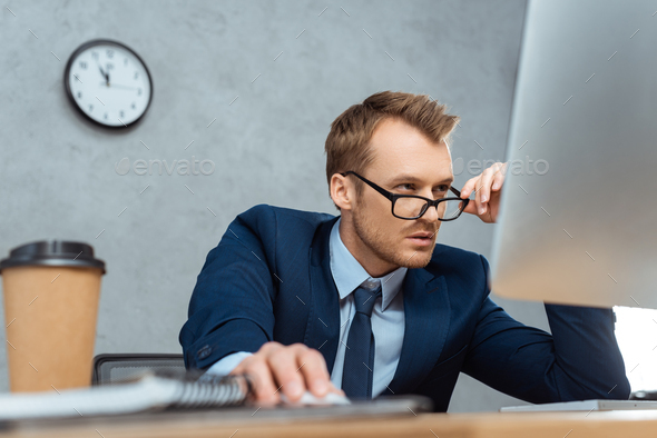 concentrated businessman adjusting eyeglasses and working at table with ...
