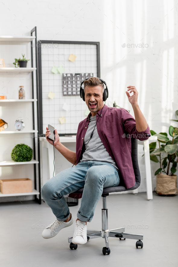 man listening music and singing loud while sitting on chair at home ...