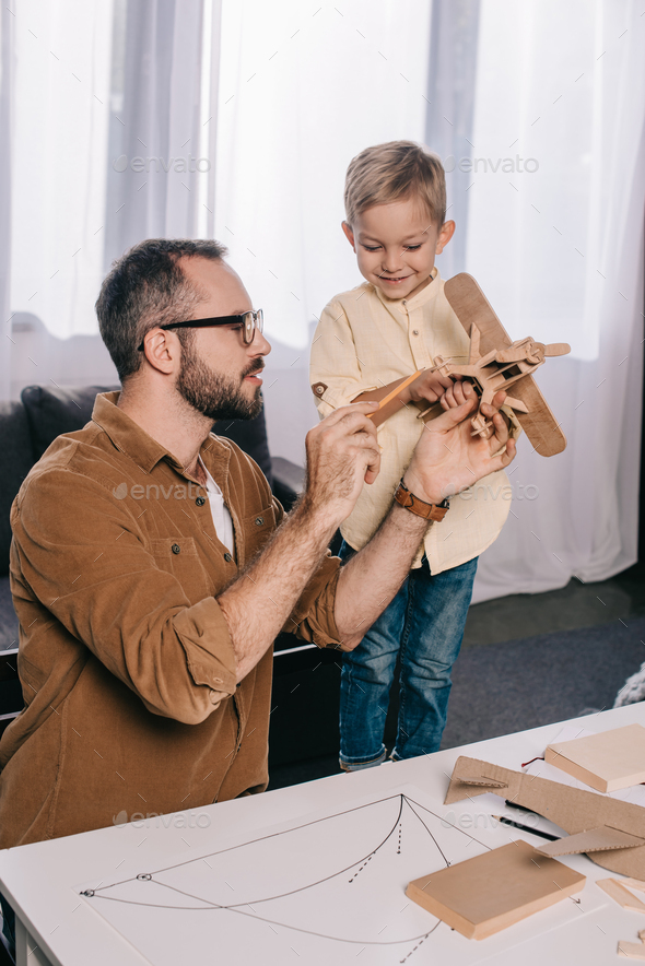 happy father and son playing with wooden plane model while modeling at ...