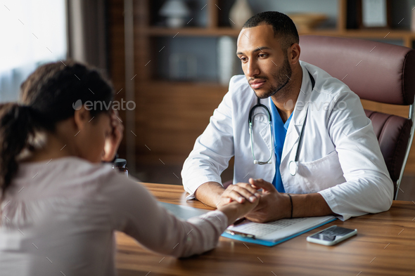 Doctor having conversation with upset black woman patient, holding hand ...