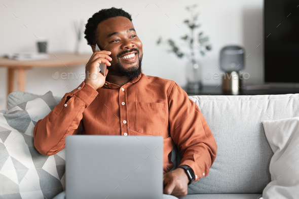 Smiling African American Guy Using Laptop Talking On Phone Indoors ...