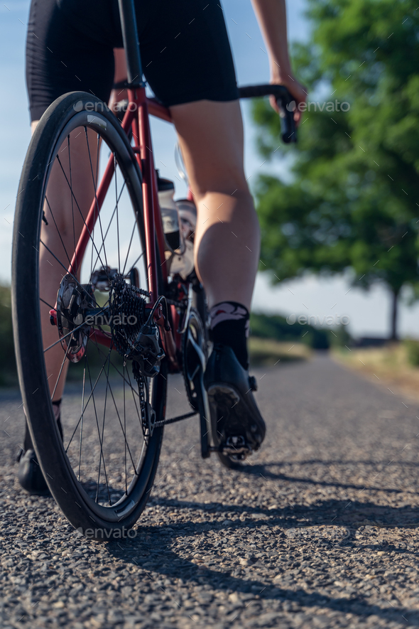 Vertical close up of a rear wheel, and the feet of a woman cyclist ...