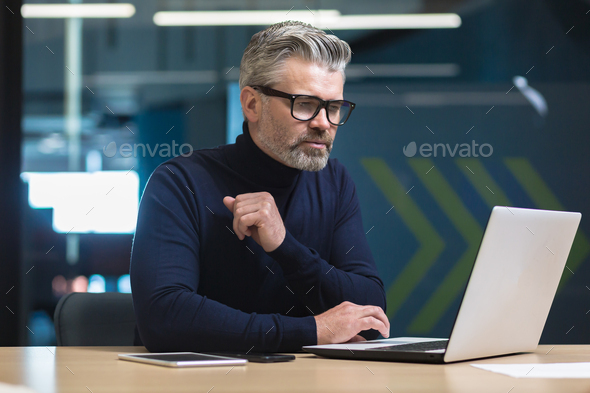 Thinking senior gray-haired businessman working in modern office with ...