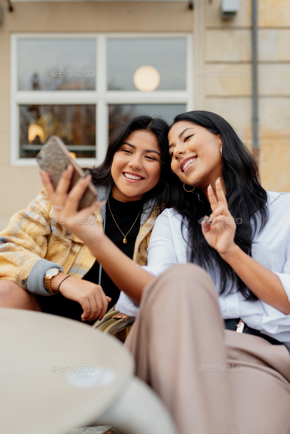 two hispanic sisters taking a picture with their smart phone in the ...