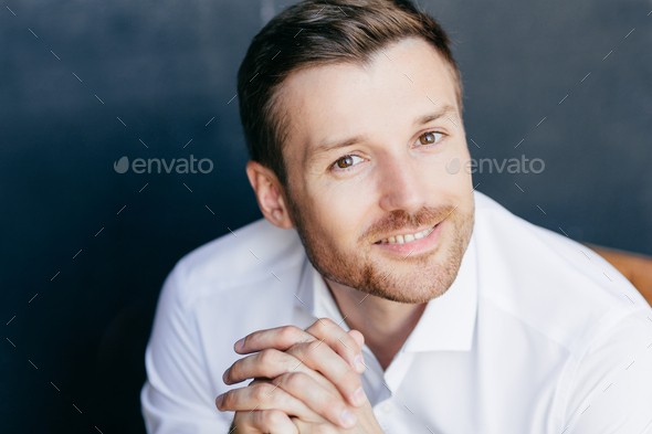 Close up portrait of handsome unshaven male with positive smile, keeps ...