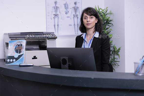 Portrait of smiling hospital receptionist standing at front desk ...