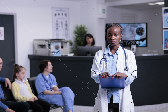 Portrait of confident medic standing in hospital reception waiting for ...