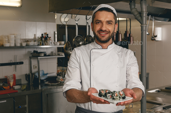 Handsome chef of japanies restaurant showing plate with sushi standing ...