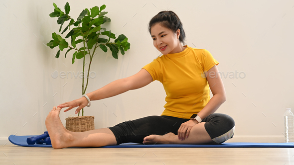 Asian woman stretching her legs on mat before morning workout at home. Healthy lifestyle concept ...