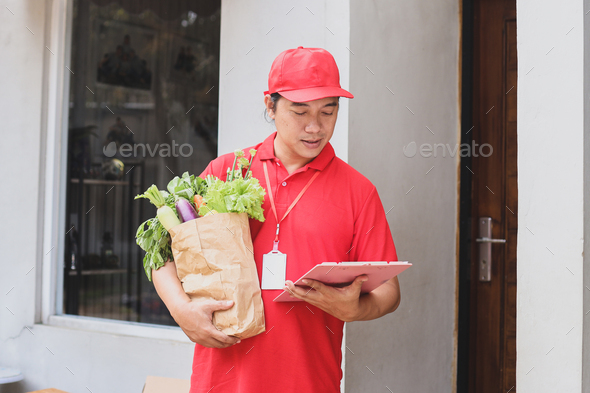 Delivery man checking document while handling bag of vegetable Stock ...