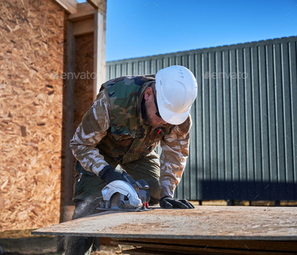 Carpenter using circular saw for cutting OSB board for building wooden ...