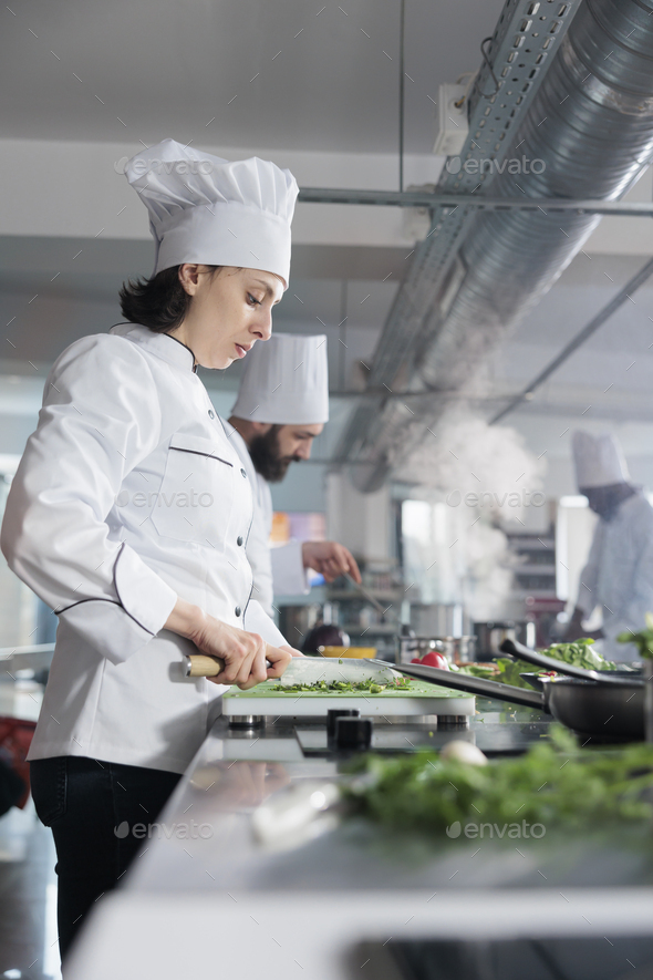 Restaurant kitchen employee chopping fresh herbs and vegetables to be ...