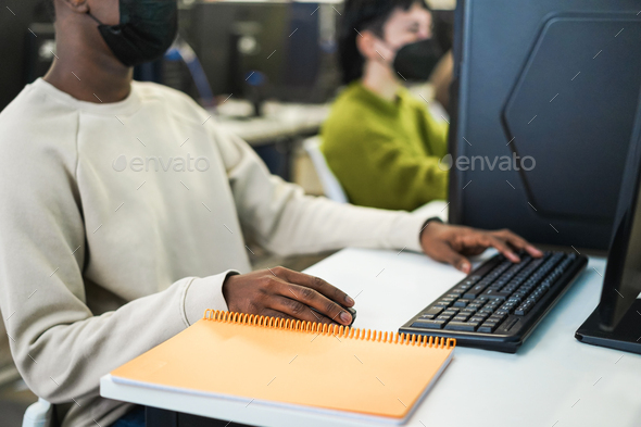 Young multiracial students using computers wearing protective mask ...