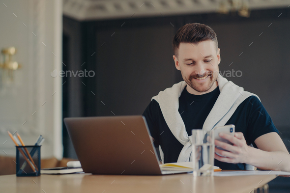 Pleasant freelancer using mobile phone while working remotely from home ...