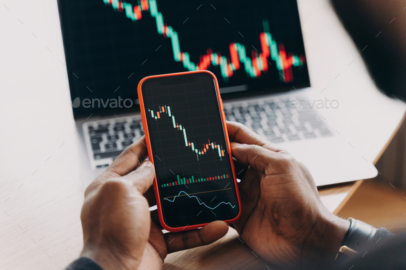 African man stock trader holding smartphone with financial charts and ...