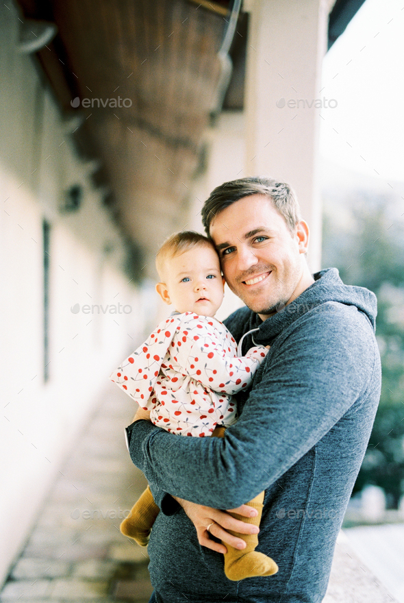 Smiling dad with a baby in his arms stands on the terrace. Portrait ...
