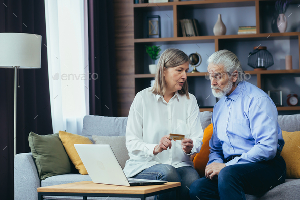 Senior couple, gray-haired retirees sitting on sofa together at home ...