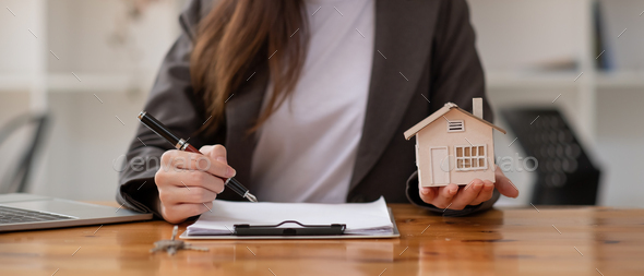 Close up businesswoman realtor taking notes and holding house model ...