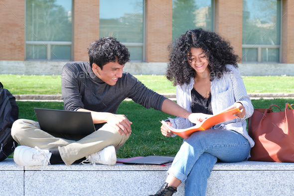 Two latin students studying from their lecture notes sitting on a wall ...