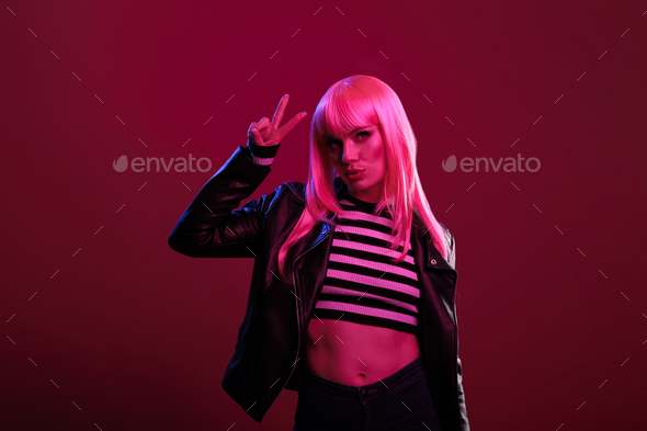 Portrait of amazing female model doing peace sign over dark pink light ...