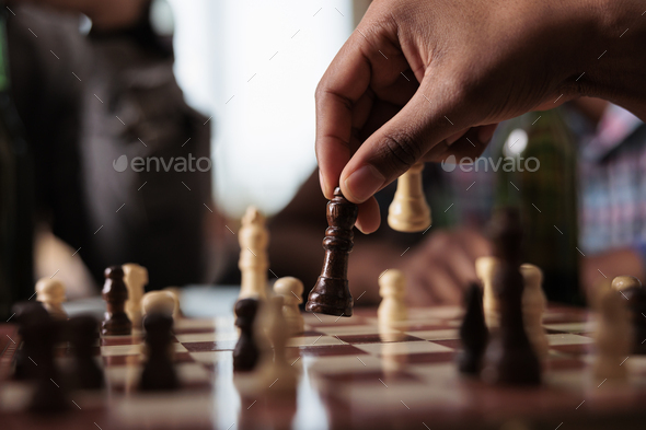 Close up of hand moving chess piece on chessboard while sitting at ...