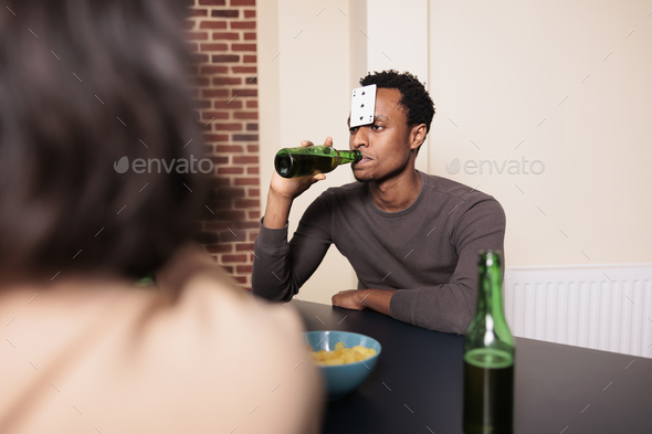 Confident young adult man with plastic card on forehead drinking beer ...
