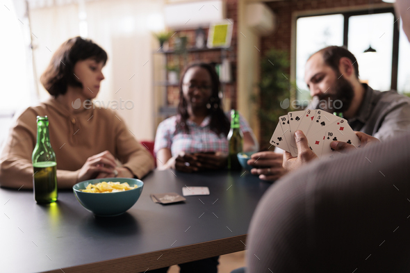 Joyful multicultural group of friends sitting at table while playing ...