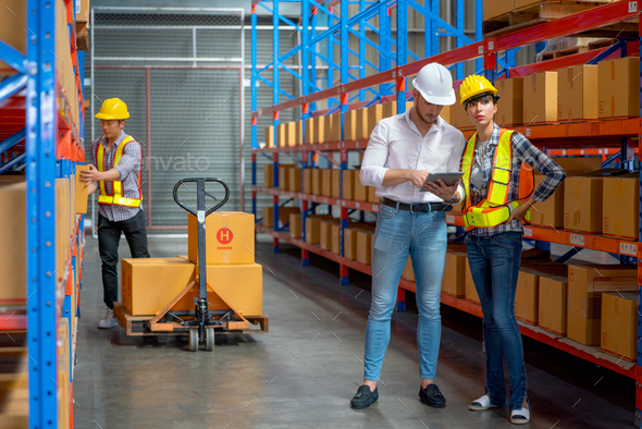 Two Caucasian warehouse worker stand and discuss together in front of ...