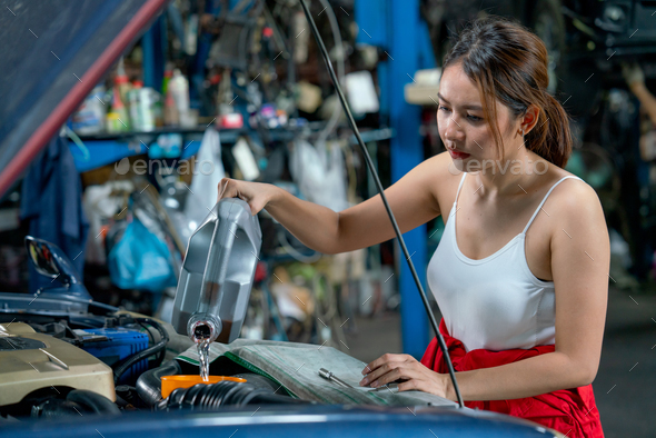 Asian mechanic woman take care engine of car by filling some chemical in the front of car and ...