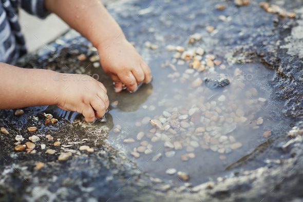 Close up of hands of little baby boy playing outdoor with small rocks ...