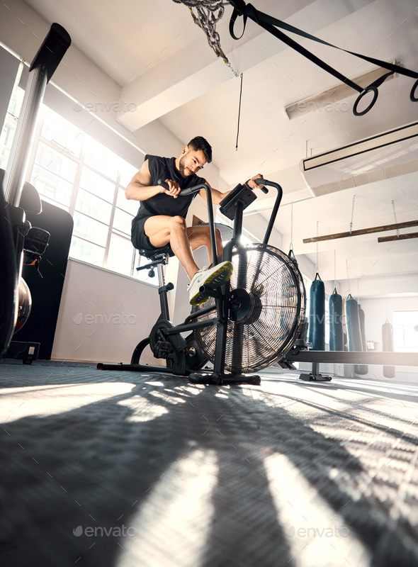 Low angle shot of a sporty young man working out on an exercise bike in ...