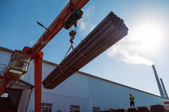 Gantry crane transporting stack of metal pipes Stock Photo by collab_media