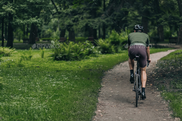Back view of muscular man riding black bike on fresh air Stock Photo by ...