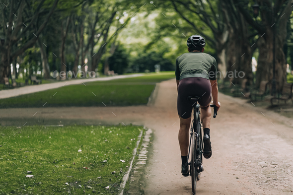 Back view active young man riding bike at green city park Stock Photo ...