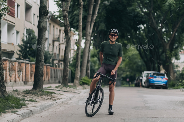 Positive cyclist with bike resting on street after ride Stock Photo by ...