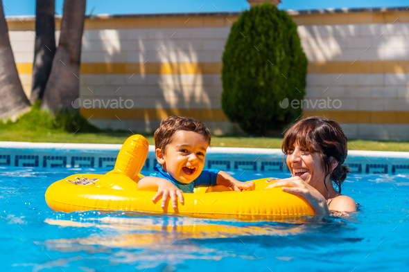 Smiling mother playing with her son with a yellow float in the pool ...