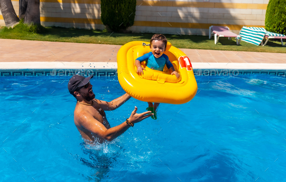 Father playing with his son with a yellow float in the pool in summer ...