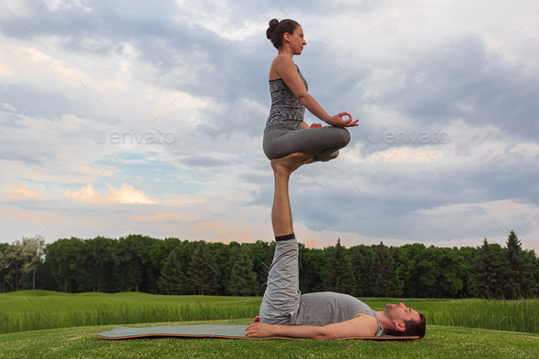 Man lying on grass and balancing woman in his feet. Young couple doing ...