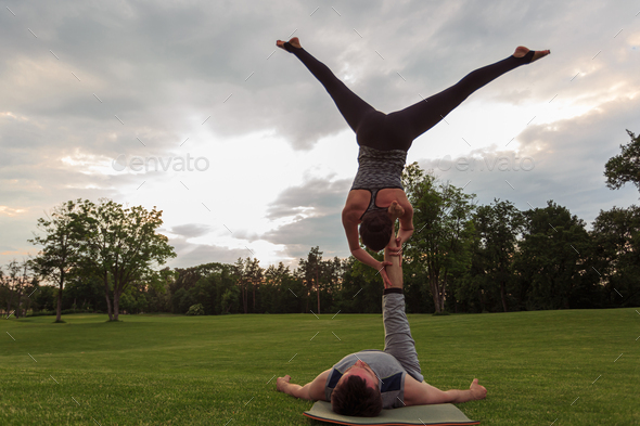 Man lying on grass and balancing woman in his feet. Young couple doing ...