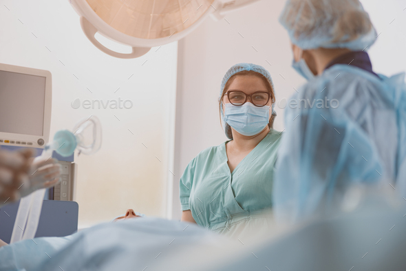 Nurse assisting doctors during surgery in operation room of modern ...
