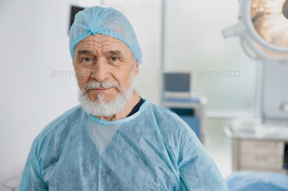 Smiling senior surgeon in uniform standing in operating room, ready to ...