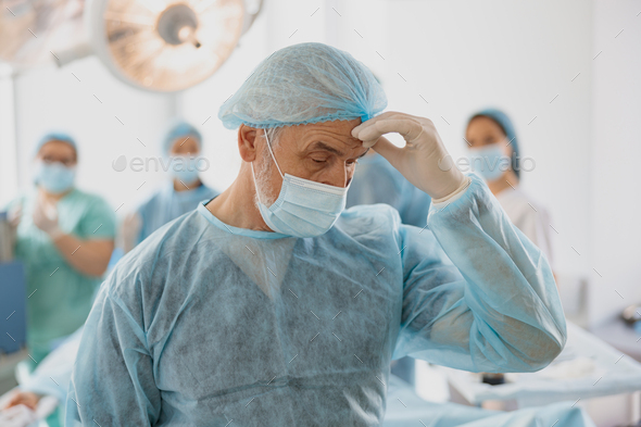 Close up of tired surgeon in mask standing in operating room after hard ...