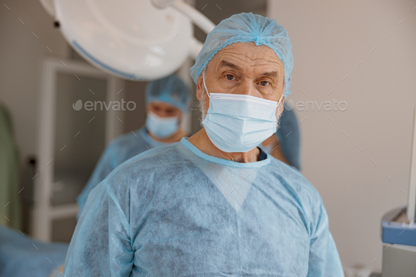 Portrait of senior surgeon standing in operating room, ready to work on ...