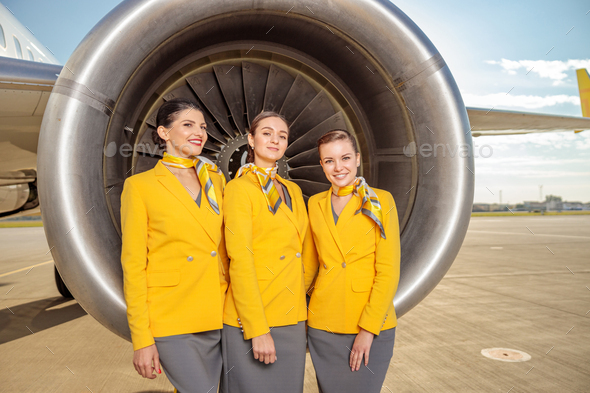 Cheerful women stewardesses standing near aircraft engine Stock Photo ...