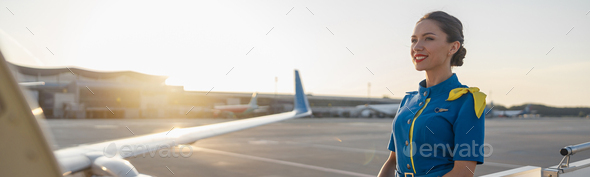 Pretty air stewardess in blue uniform smiling away, standing outdoors ...