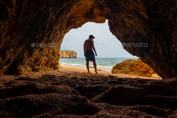 A man in the natural cave in the Algarve in summer on the beach at ...