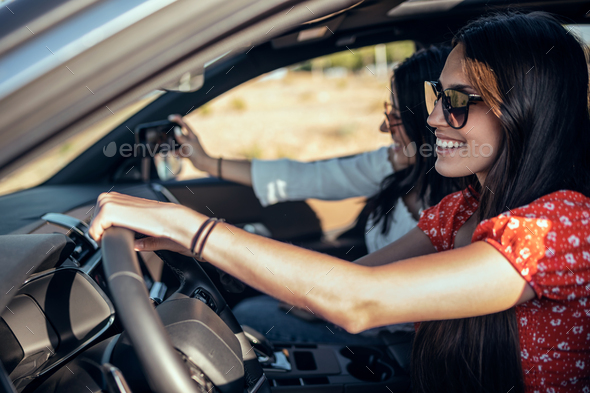 Pretty young women taking a photo while driving a car on road trip on ...
