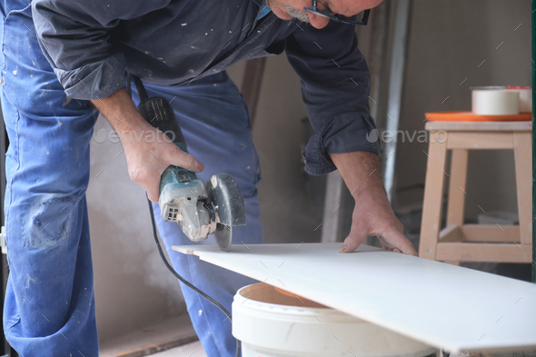 Senior constructor worker cutting a white ceramic tile with a radial ...