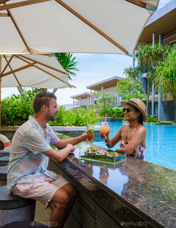 Couple sitting on the bar in a swimming pool drinking cocktails, eating ...